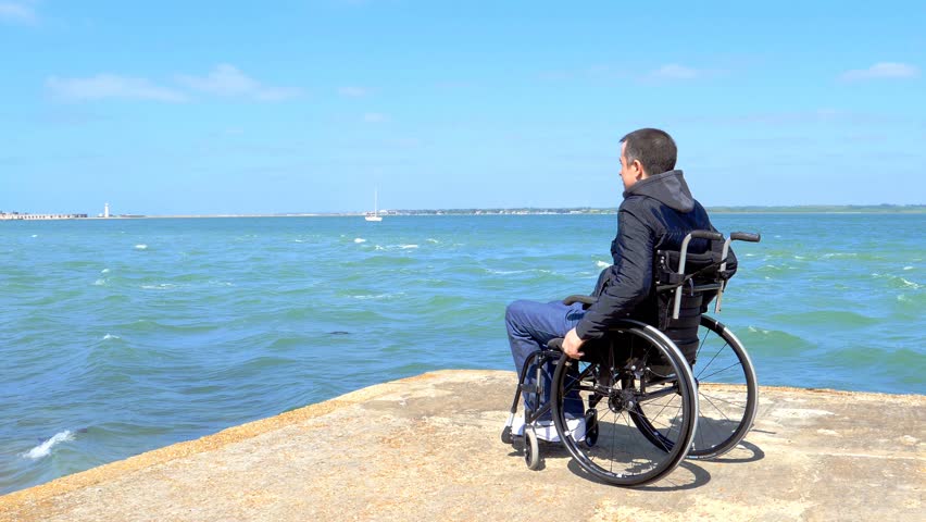 Lonely Disabled Woman Sits And Thinks In Her Wheelchair At The Water's ...